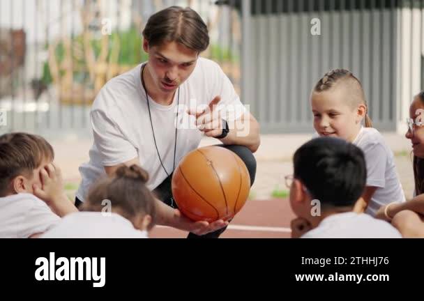 Sporty coach catching ball and explaining game strategy to primary ...
