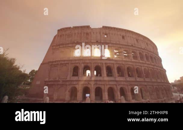 Bright sunset light illuminates large Colosseum built in Rome near dark ...