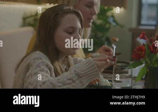 Young girl eats tasty dish on family dinner with mother in modern cafe ...