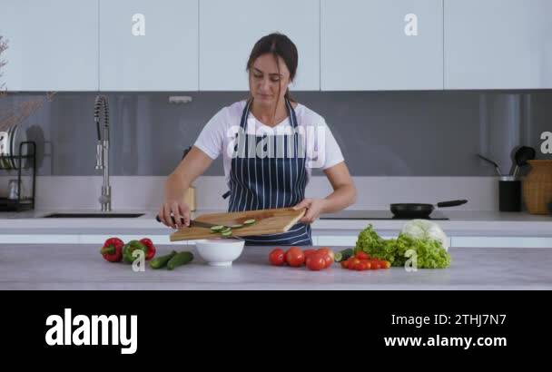 young female chef in an apron cooking lunch of fresh vegetables while ...