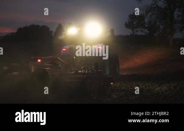 Tractor plowing and harvesting working in a field at night on a farm ...