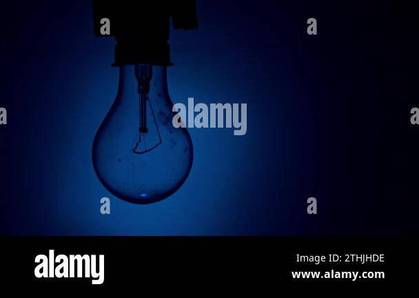 Light bulb flashes on a blue background in the dark. Slow turning on ...