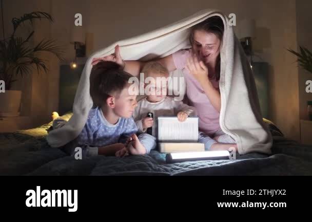 Two boys and mother in pajamas reading bedtime story book in bed at ...