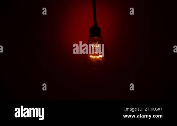 Light bulb staggers on a red background in the dark. Slow turning on ...