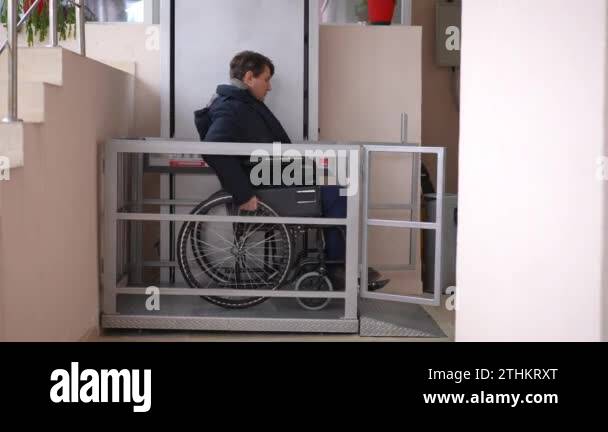 Wide shot man riding wheelchair leaving lift platform entering building ...