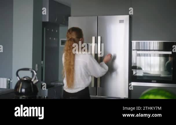 Young woman taking orange from fridge throwing it up. Girl getting ...