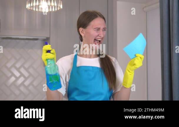 Beautiful brunette young woman in blue apron holding cleaning products ...