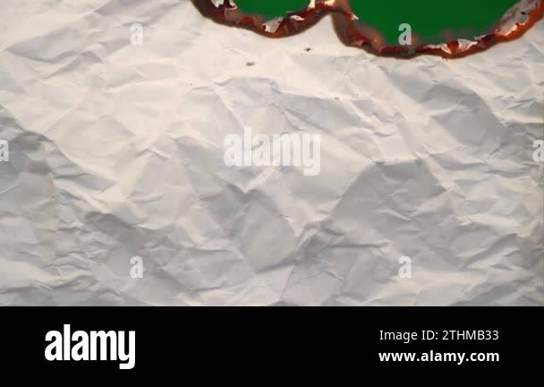 White paper burns from above on a green background copy space. The ...