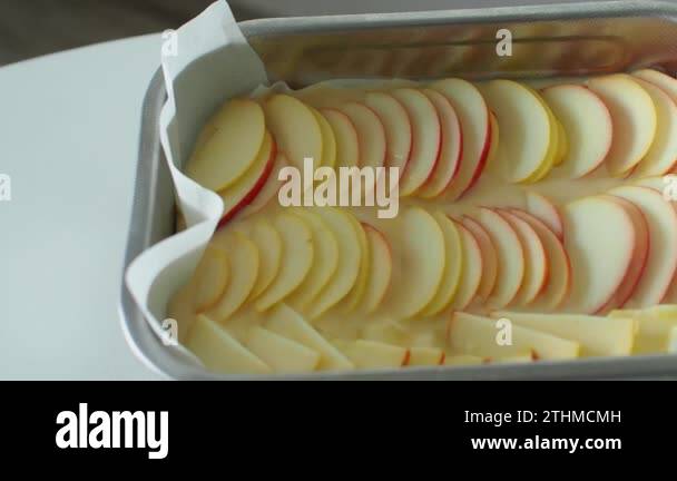 Woman lays out slices of apples in pie baking dish, close up. The ...