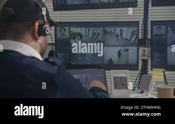 Security officer in headset monitors CCTV cameras on computer in ...