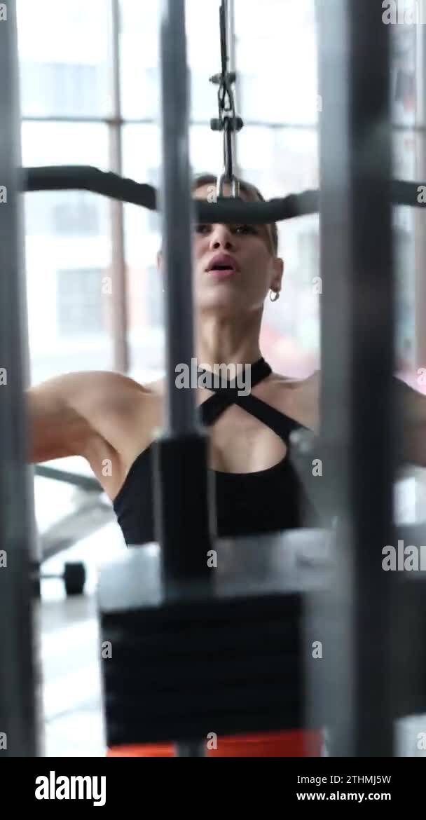 Vertical video, woman trains the back muscles in the gym, she pumps the ...