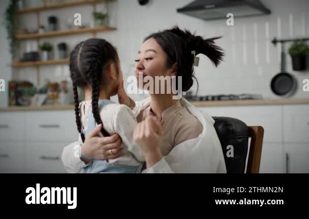 Loving Mom Hugging Her Daughter. Happy Asian mum and girl hug and kiss sitting at home. 4K Stock ...