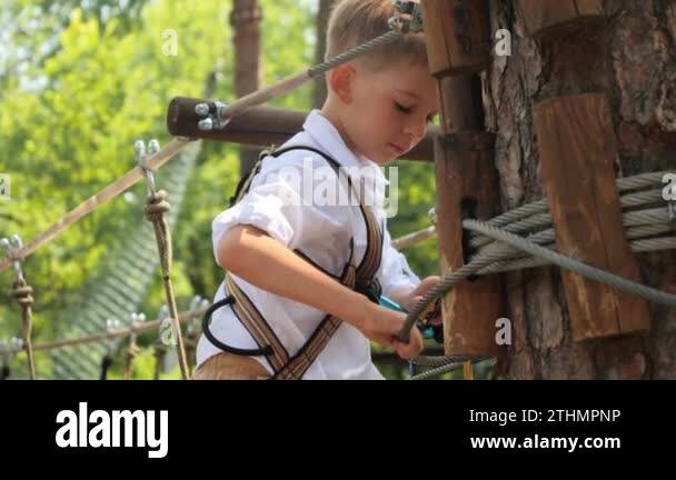 Little boy adjusting safety rope and hook in rope adventure park ...