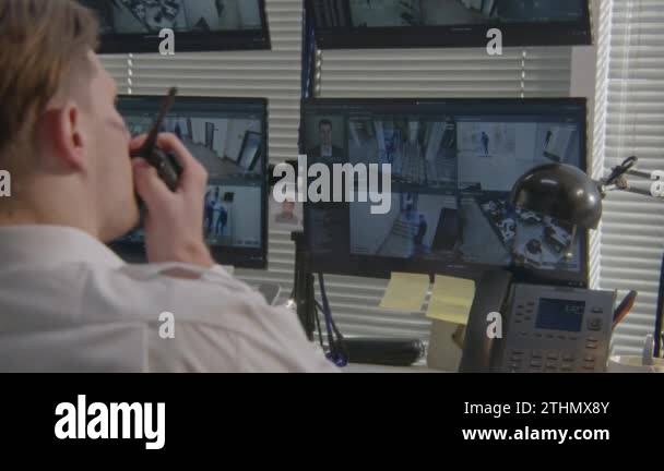 Security officer monitors office CCTV cameras on computers, uses walkie ...