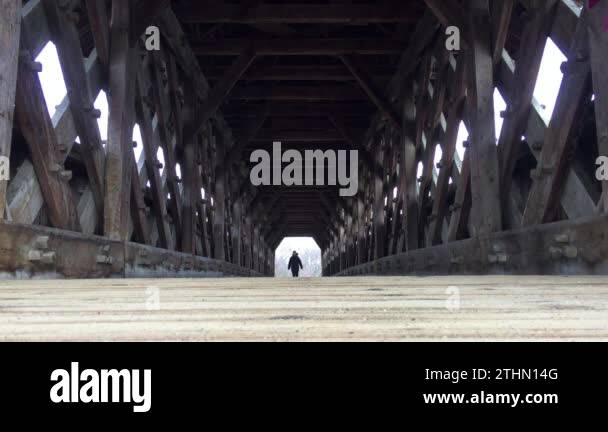 Low wide angle on pedestrian coming into view at end of covered bridge ...