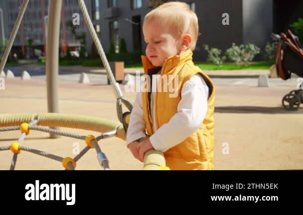 Upset crying baby boy standing on the playground at swing. Children ...
