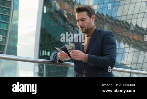 a successful businessman in a suit stands near a skyscraper and counts ...