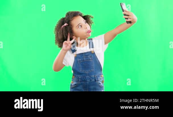 Silly little girl, selfie and peace sign on green screen with goofy facial expressions against a ...