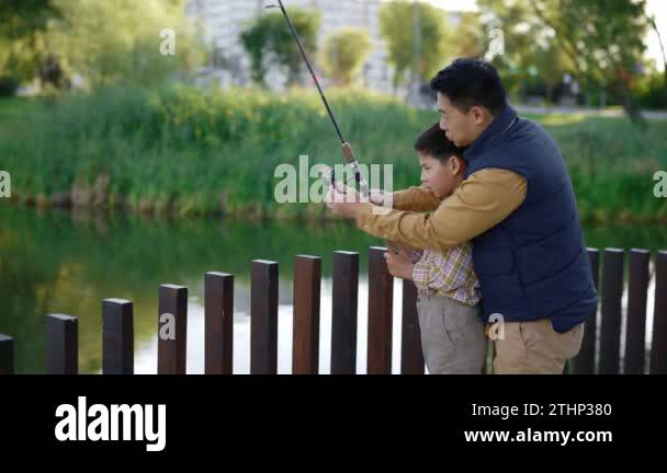 Asian dad shows his son how to cast a fishing rod on practice, gives ...