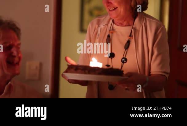 Older couple celebrating birthday with cake and candles. WIfe bringing ...