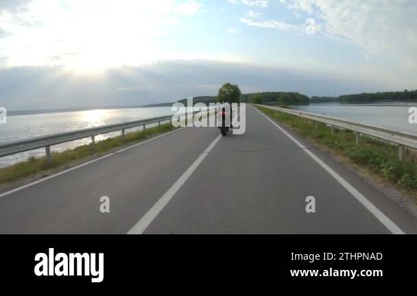 Biker riding on modern sport motorbike through road near lake ...