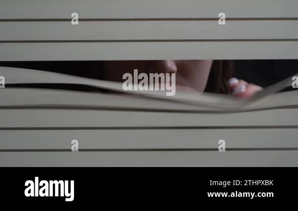 Close up front portrait from indoors of young girl pushing blinds at ...