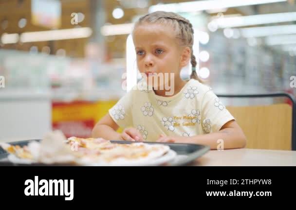 Child eat pizza sitting on the table at food court in supermarket ...