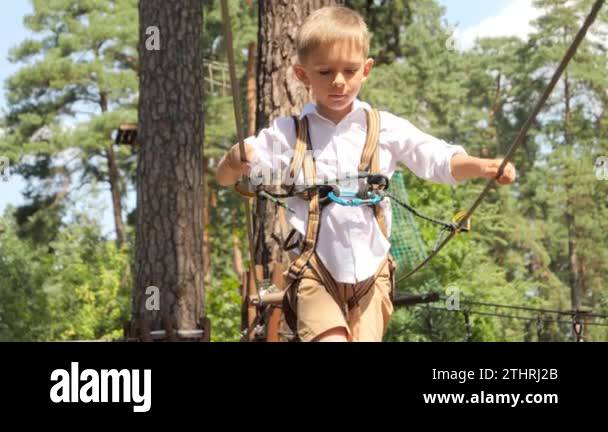 Portrait of little boy walking over rope strung between trees in scout ...
