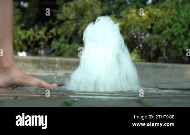 Barefoot young woman washing her feet and hands in pedestrian fountain ...