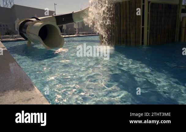 Cascading water splashing at the exit of a water slide into a sunlit ...