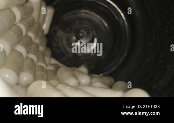 White capsule tablets in a black jar that rotates. they fall out of the ...