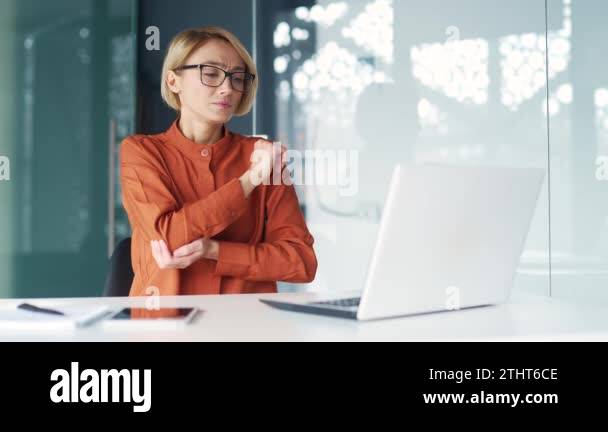Tired young woman suffering from elbow pain while working on laptop ...