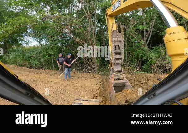 POV of hydraulic excavator operator; bucket scoops a load of dirt, man ...