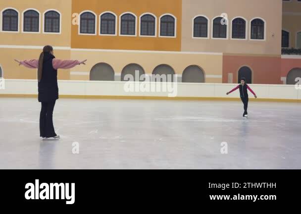 Back view of a female figure skating coach looking at her pupil and ...
