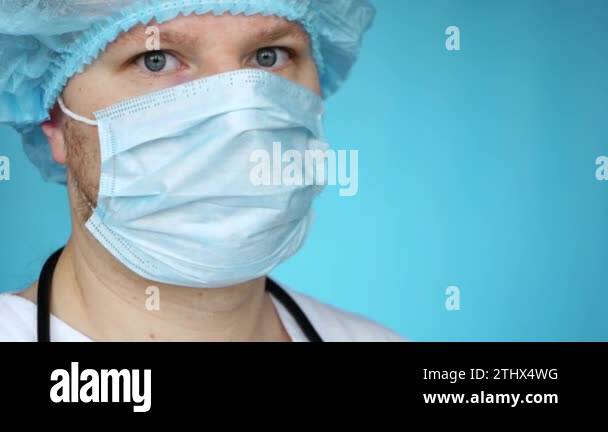 Portrait A doctor in uniform and in a medical mask looks at the camera ...