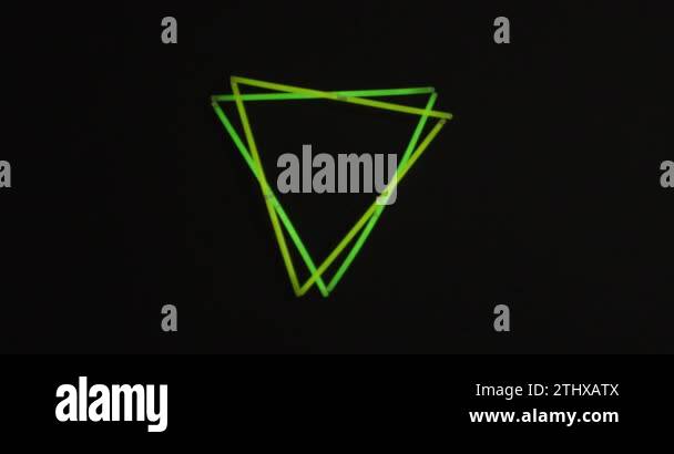 Animation of green neon glow sticks forming triangles over black background with copy space ...