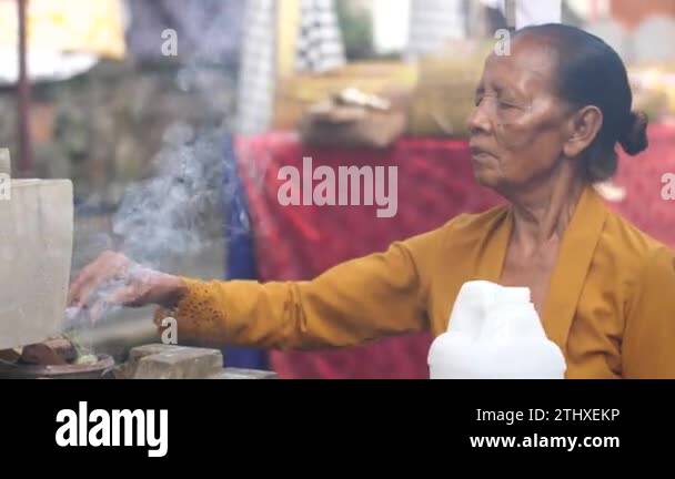 Old woman in Bali tends to offerings and burning incense at her temple ...