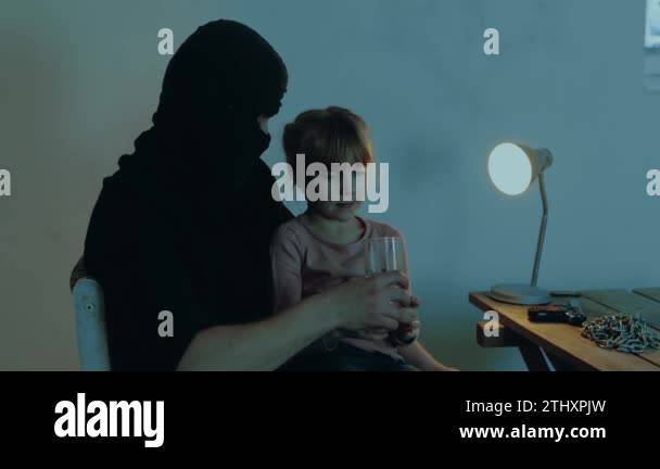 Male kidnapper serving a glass of water to little hostage girl. Robber ...