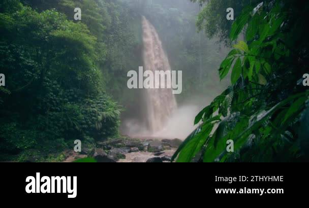Epic waterfall flows from a high cliff in tropical green forest ...