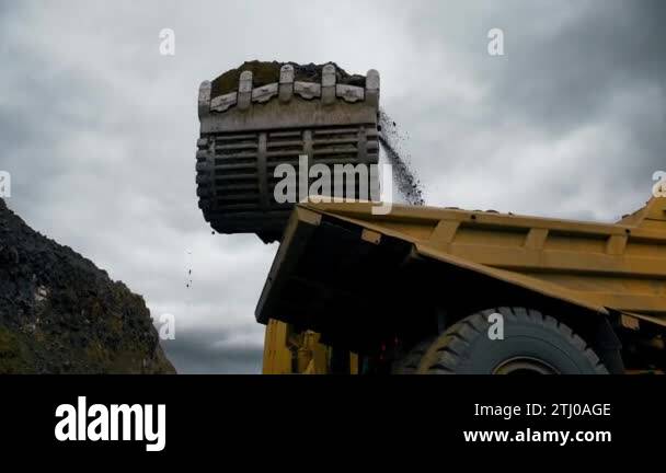 A yellow excavator scoops up ore with a large bucket and transfers it ...