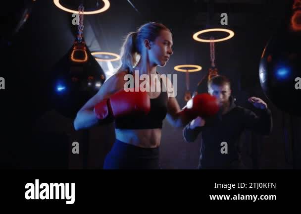Male boxer trainer shows to the woman wearing red boxing gloves how to ...