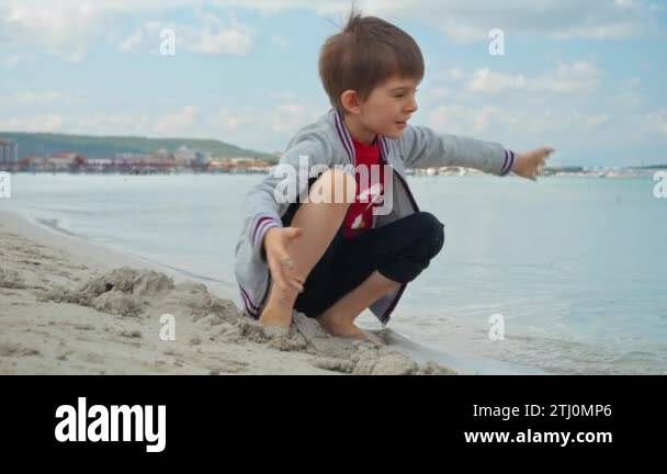 Boy sitting on the sea beach, digging and playing with sand. Concept of ...