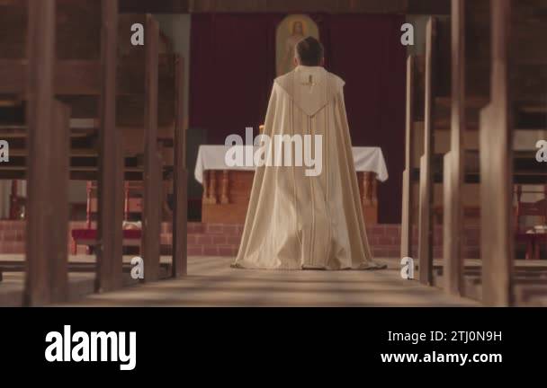 Rear view slowmo of priest in long white cape cloak praying, standing ...