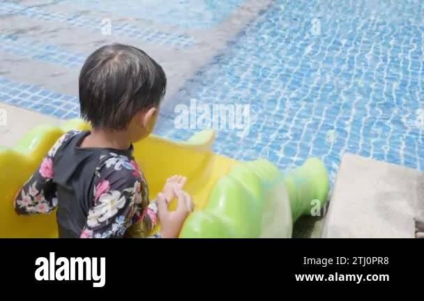Asian child little boy playing outdoor swimming pool on water slider bar toy, Happy kid playing ...