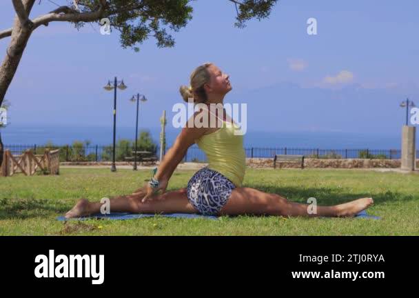 An adult woman doing yoga on nature - sitting on splits on yoga mat and ...