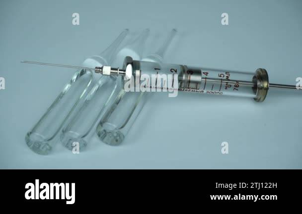A glass rare Soviet syringe with a needle lies on transparent ampoules ...