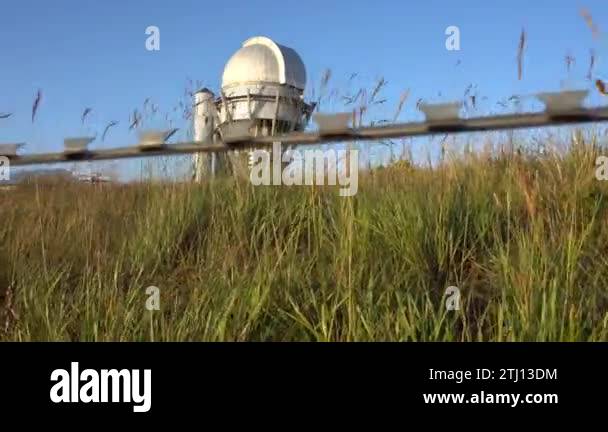 A large observatory is protected by a barbed fence. There is a long ...