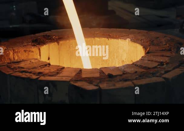 A stream of molten metal flows into a melting furnace. Steam and sparks ...