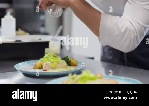 Chef adding salt and spices from grinder to dishes on plates while ...