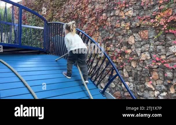 Little girl climbs a slide holding on to a rope and slides down. High ...
